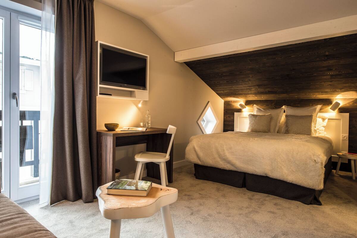 Quarto com cama, escrivaninha, cadeira e televisão.