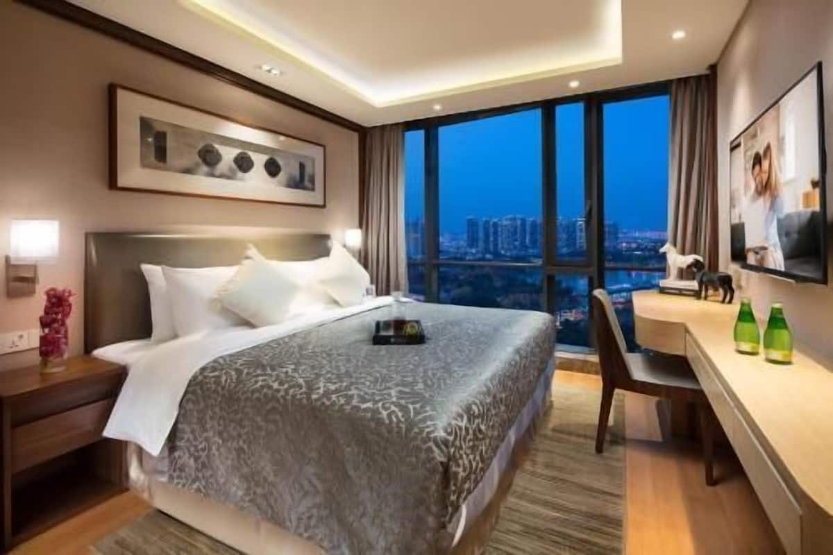 Quarto de hotel com cama, escrivaninha, cadeira e uma ampla janela com vista para a cidade.