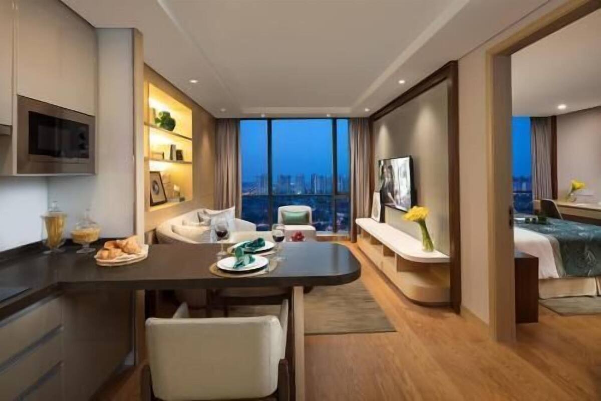Quarto de hotel moderno com área de refeições, sofá, cama e vista para a paisagem urbana.