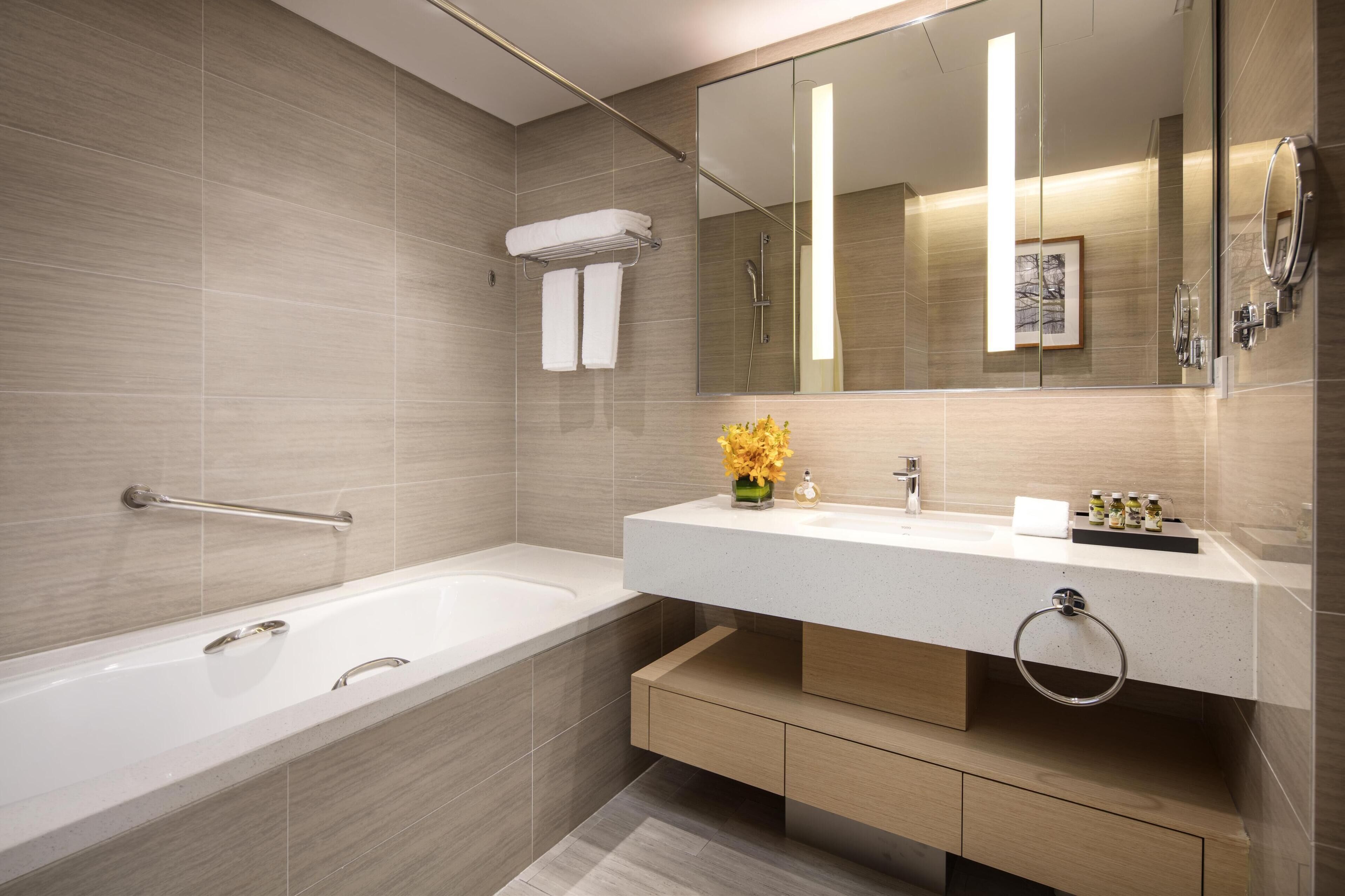 Uma casa de banho moderna com banheira, toucador com espelho e porta-toalhas.