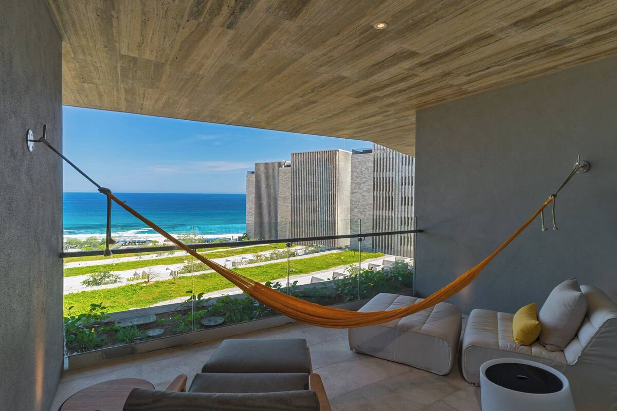 Uma varanda moderna com uma rede, um sofá e vista para o mar e edifícios.