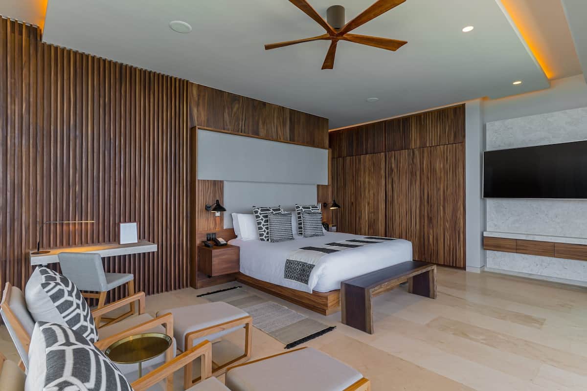 Quarto moderno com uma cama grande, paredes de painel de madeira, uma escrivaninha e uma televisão.
