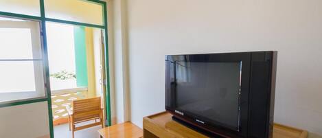 Quarto com uma grande televisão de tela plana sobre um suporte de madeira, uma mesa de madeira e uma cadeira.