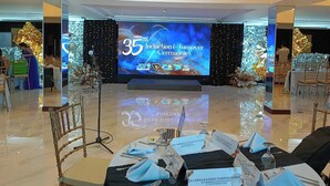 Um espaço para eventos formais com palco, cadeiras e mesas organizadas para uma cerimônia de posse.