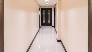 Um corredor comprido e estreito, com paredes em tom bege e uma porta de moldura preta no final.