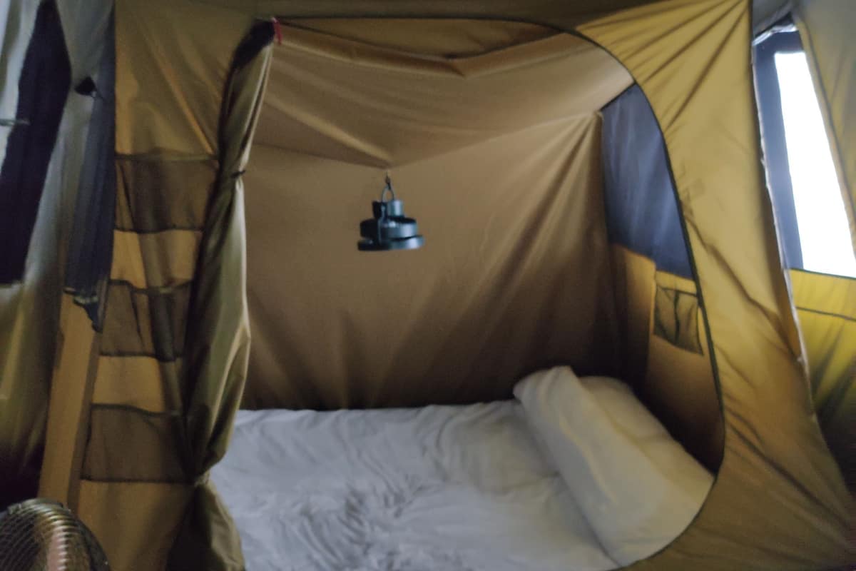 Uma tenda com uma cama, uma luminária pendente e uma janela.