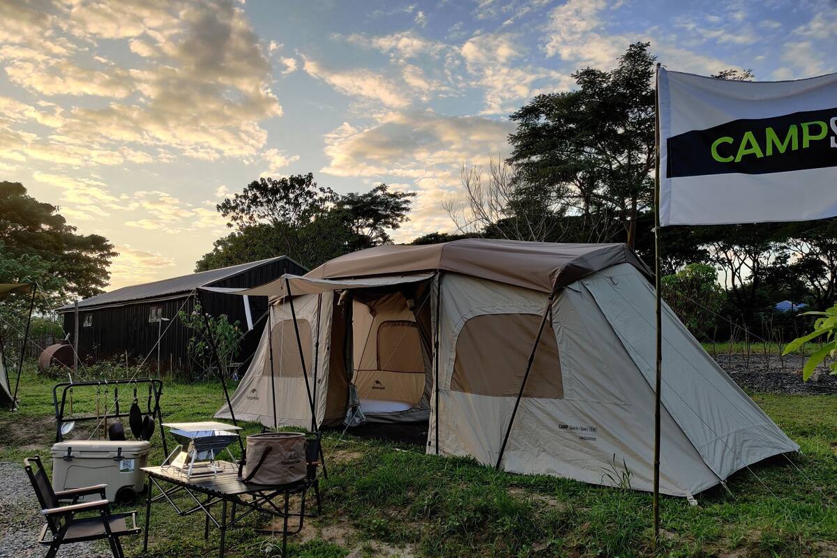 Um camping com uma tenda, uma mesa e cadeiras, e uma bandeira.