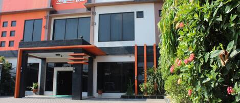 Um hotel moderno com fachada marcante em laranja e branco, grandes janelas e uma área de jardim bem cuidada.