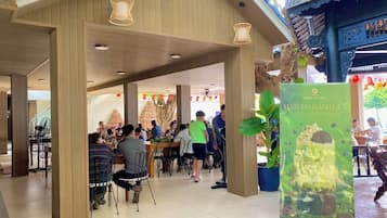 Restaurante com pilares de madeira, mesas e cadeiras, e um cartaz verde publicando um chá matcha.