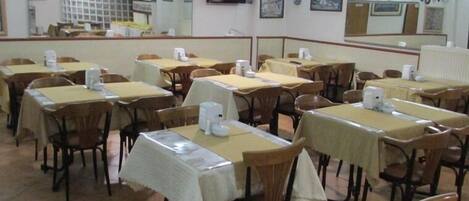 Uma área de refeições com várias mesas e cadeiras, piso ladrilhado e decorações nas paredes, incluindo pratos e quadros.