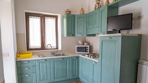 Cozinha com armários azul-turquesa, micro-ondas, fogão e televisão sobre um móvel.