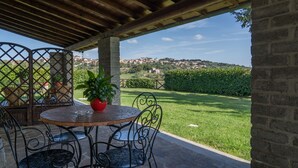 Um alpendre coberto com uma mesa redonda e cadeiras, uma planta em vaso e vista para uma cidade ao longe.