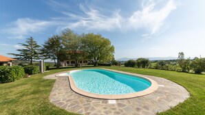 Piscina com deck de pedra, rodeada por um gramado bem cuidado e árvores.