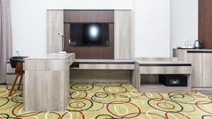 Quarto de hotel moderno com televisão de tela plana fixada em uma parede revestida de madeira, uma pequena escrivaninha com cadeira, máquina de café e um móvel de armazenamento sob a mesa.