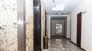 Um corredor com piso de mármore, uma lixeira e uma porta no final.