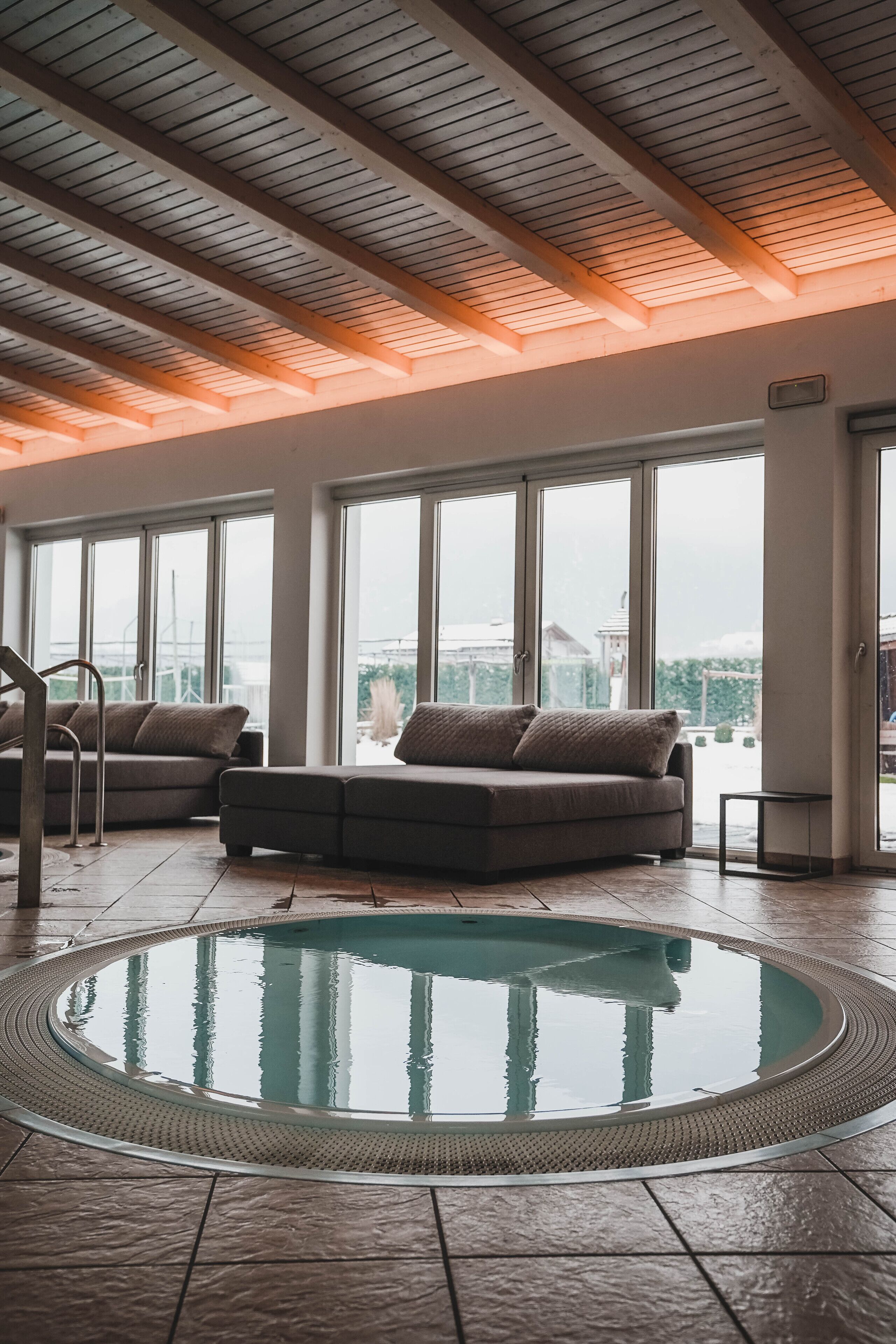 Uma área interna de piscina moderna com uma janela grande, uma piscina e um sofá.