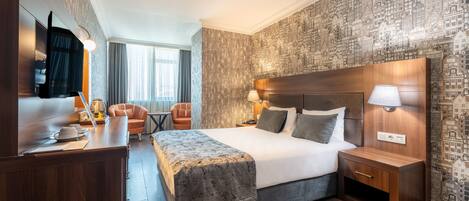 Quarto de hotel com uma cama grande, mesas de cabeceira, escrivaninha com cadeira, televisão e papel de parede estampado.