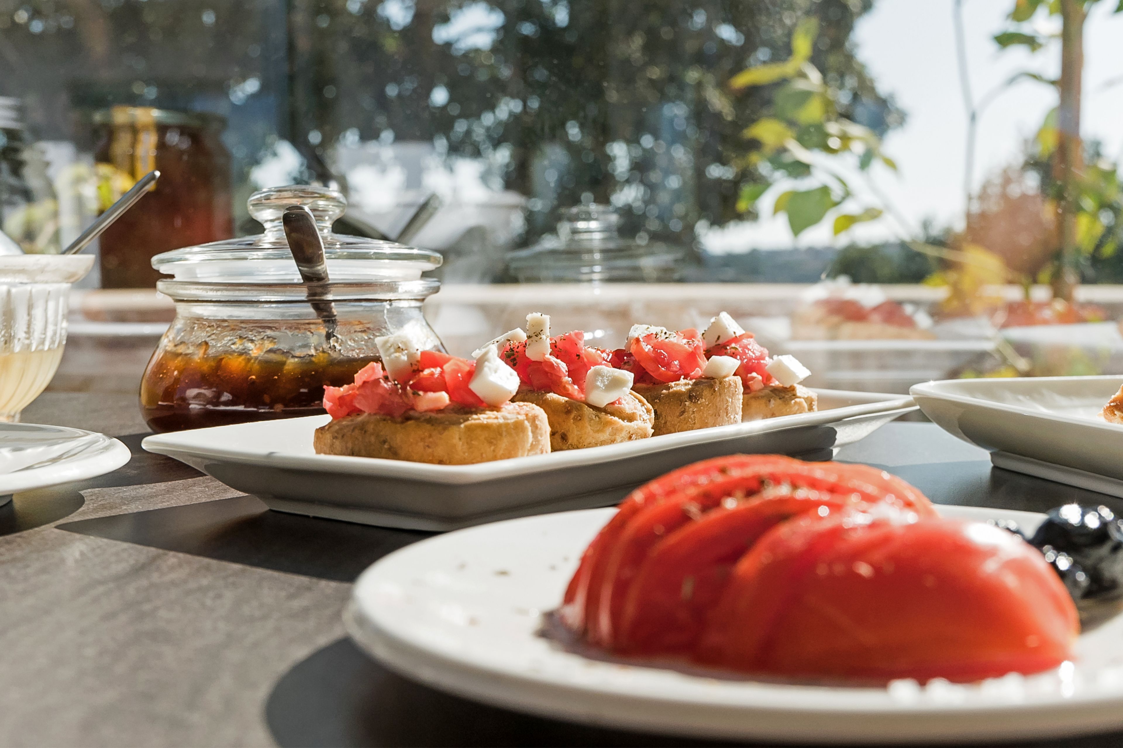 Uma mesa com diversos alimentos, incluindo fatias de tomate e um pote de vidro com uma colher.