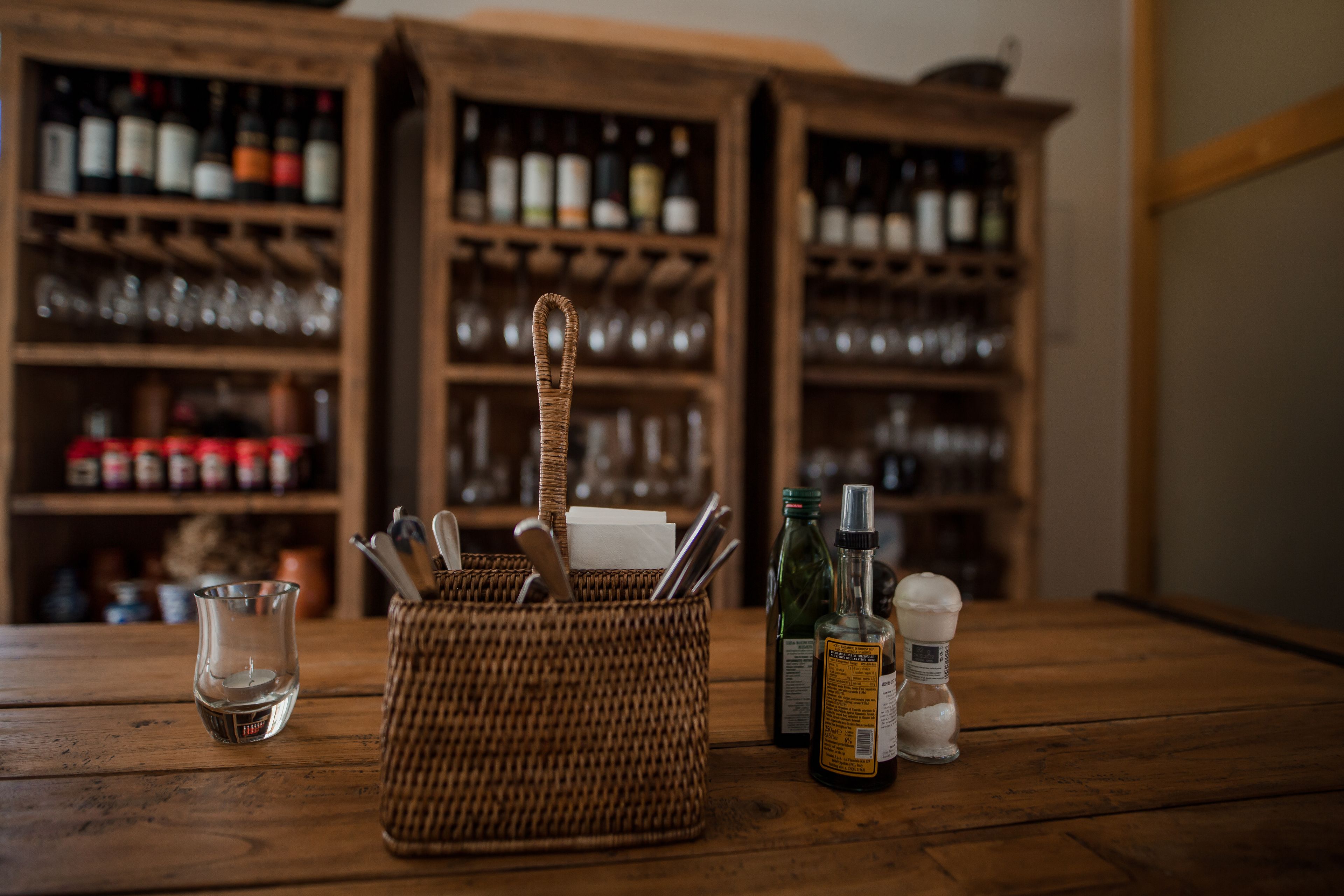 Uma mesa de madeira com uma cesta de vime contendo utensílios, um copo pequeno e duas garrafas.