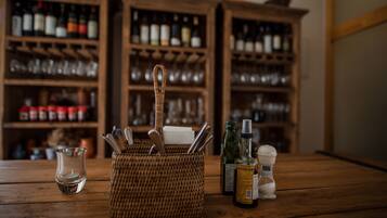 Uma mesa de madeira com uma cesta de vime contendo utensílios, um copo pequeno e duas garrafas.