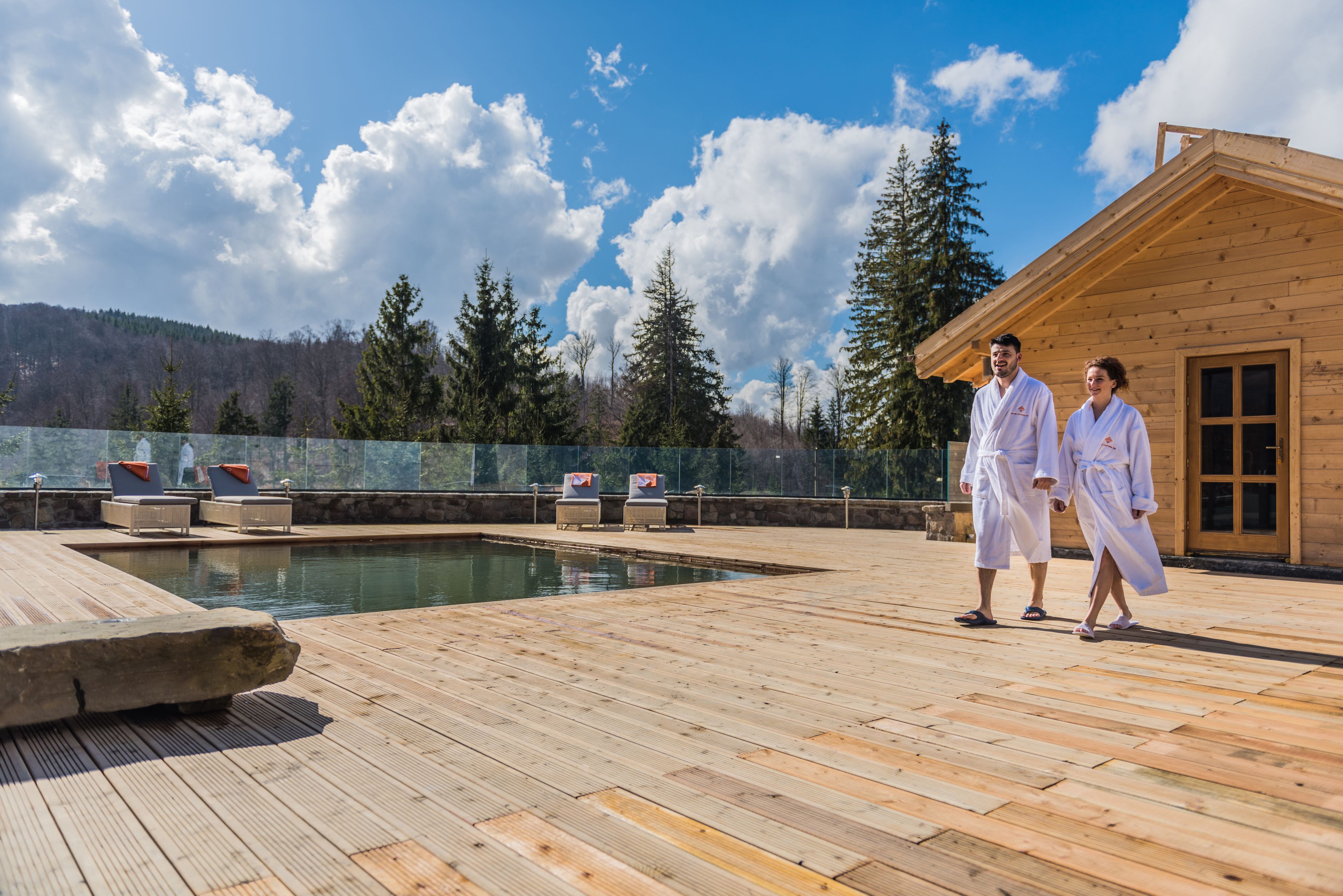 Um deck de madeira com piscina, cadeiras de descanso e um chalé de madeira.