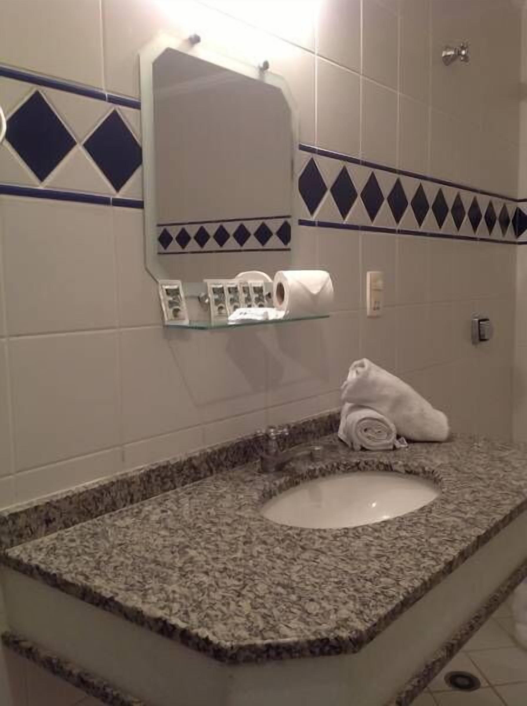 Casa de banho com lavatório de bancada em granito, espelho e porta-toalhas.