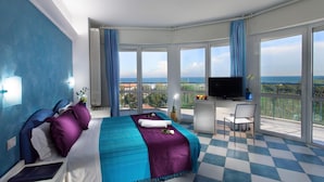 Quarto com cama grande, escrivaninha, televisão e varanda com vista.