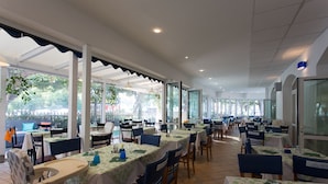 Um restaurante espaçoso com várias mesas e cadeiras, grandes janelas e uma área de estar coberta ao ar livre.