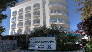 Hotel com vários andares, varandas, placa indicando piscina e garagem, e céu azul claro.