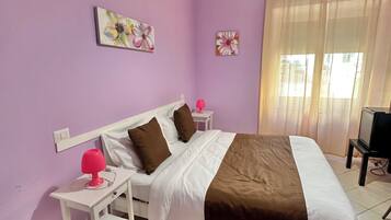 Quarto com cama, mesas de cabeceira, abajur e duas pinturas florais na parede.