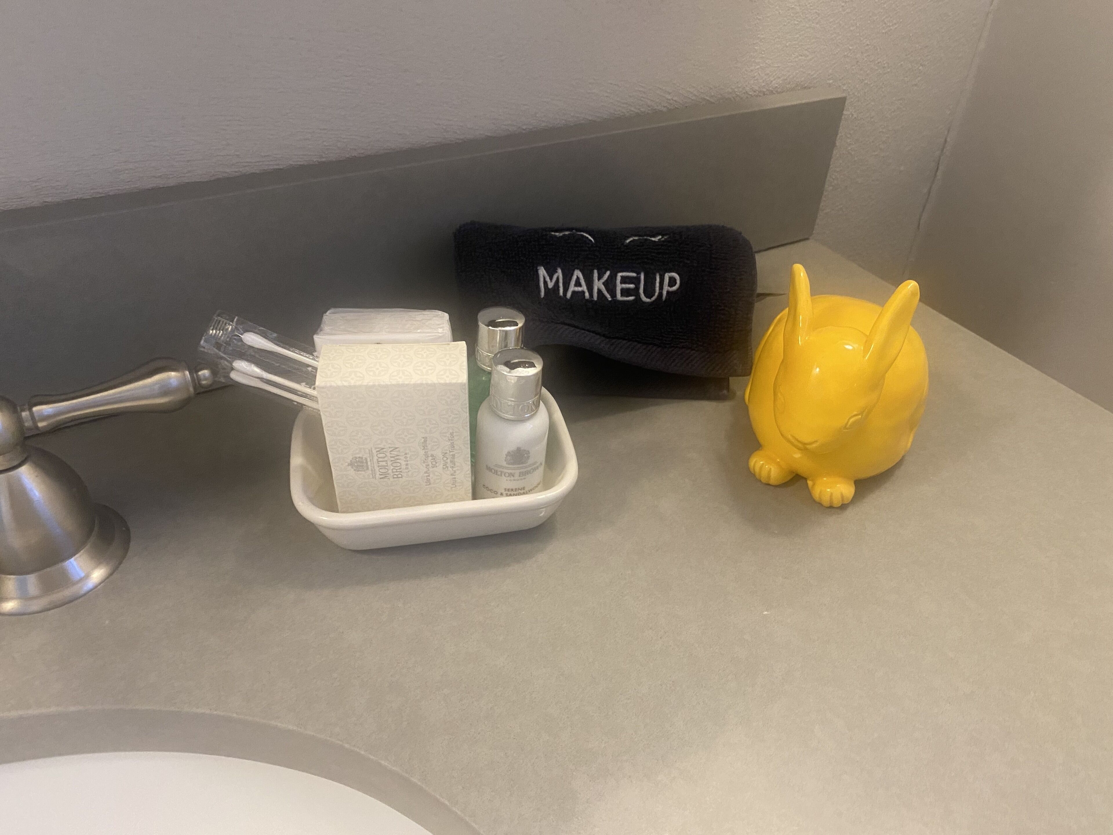 Uma toucador de banheiro com uma bolsa de maquiagem, itens de higiene pessoal e uma figurinha de coelho amarelo.