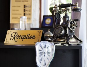 Uma mesa de recepção com um telefone antigo, um relógio e uma placa que diz 'Reception'.