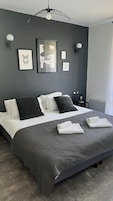 Quarto moderno com cama grande, paredes cinzentas e obras de arte.