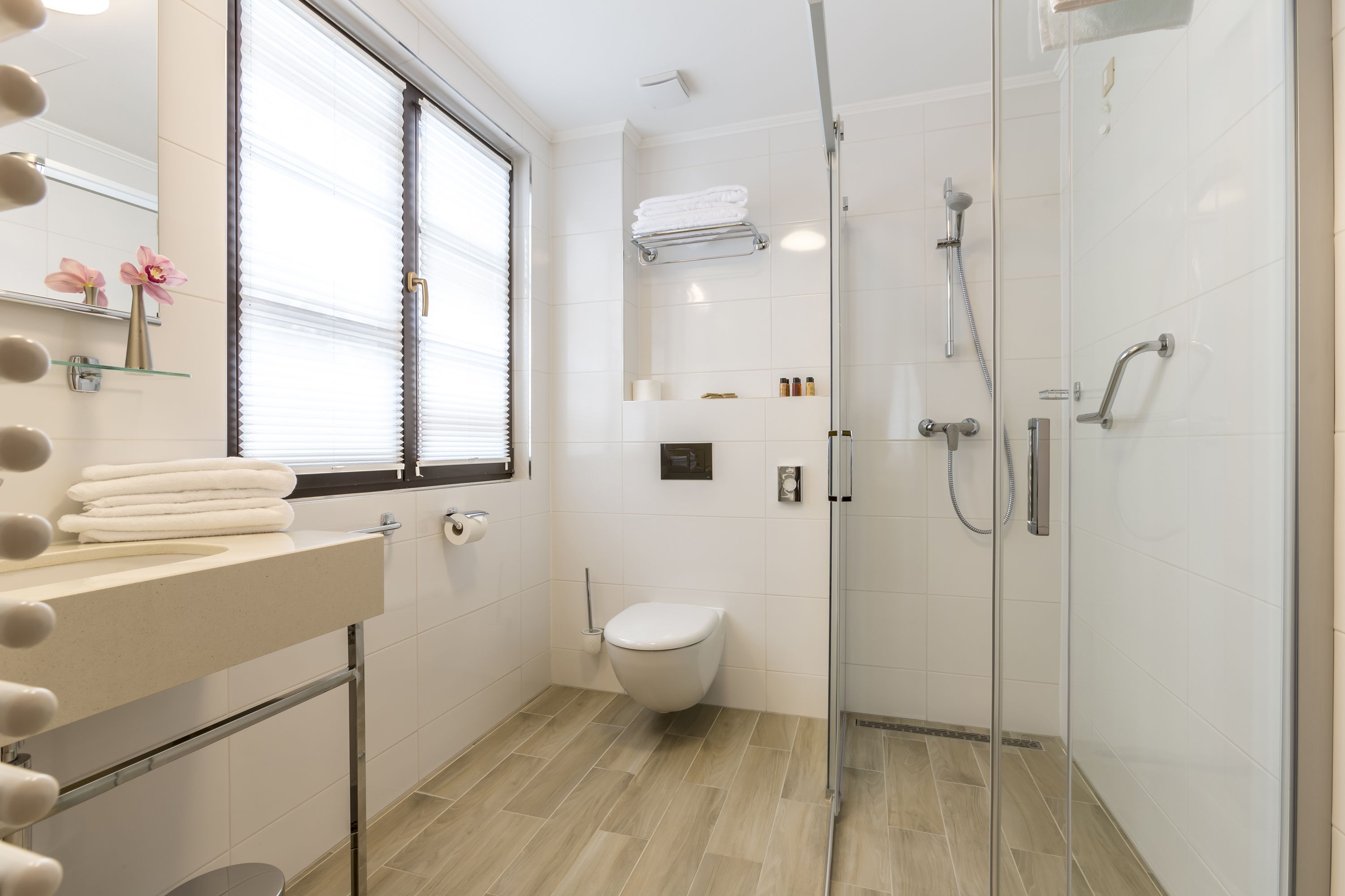 Uma casa de banho moderna com cabine de chuveiro em vidro, sanita, toucador com espelho e janela com estores.