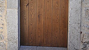 Uma porta de madeira com três painéis retangulares, emoldurada por um arco de pedra.