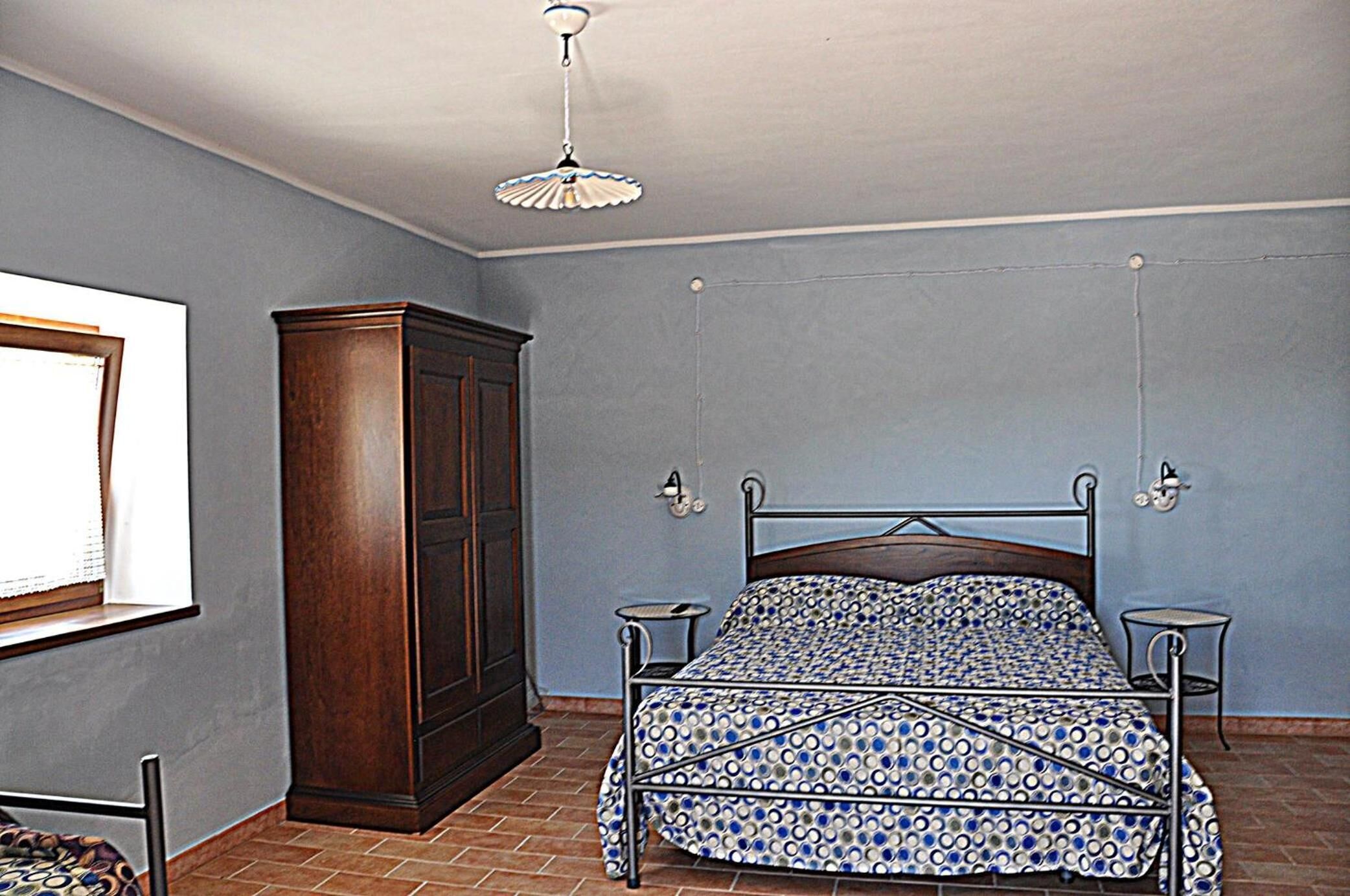 Quarto com cama, guarda-roupa, janela e luminária suspensa.