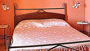 Um quarto com teto de madeira, cama com colcha estampada, mesa de cabeceira e luminária suspensa.
