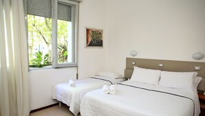 Quarto de hotel com duas camas, uma janela com cortinas, um quadro na parede e vista para o verde lá fora.