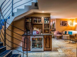 Um hall de hotel com uma escadaria, um minibar, uma área de estar com sofá e poltronas, e um quadro fixado na parede.