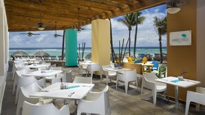 Um restaurante à beira-mar com mesas e cadeiras brancas, teto de madeira e vista para o oceano.