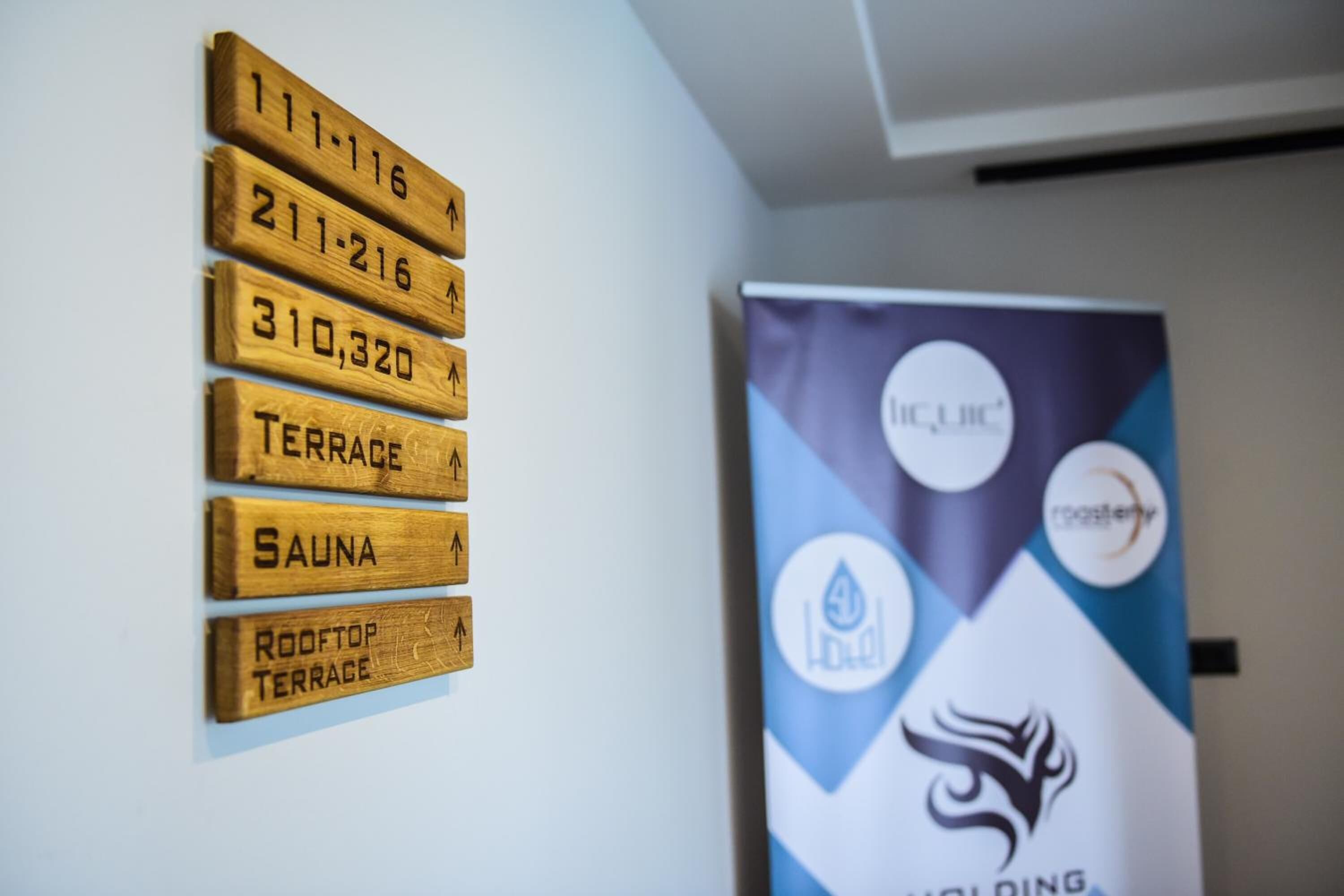 Placas de madeira com números e nomes de quartos, um cartaz com logotipos e uma saída de ventilação no teto.