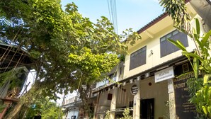 Um hostel com uma placa indicando que não é hostel lao, uma motocicleta estacionada em frente e uma grande árvore oferecendo sombra.