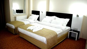 Uma cama de casal com lençóis brancos, uma mesa de cabeceira com abajur e uma janela com persianas.