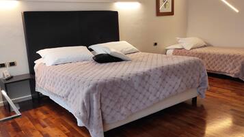 Quarto de hotel com duas camas, mesa de cabeceira, luminária na parede e piso de madeira.