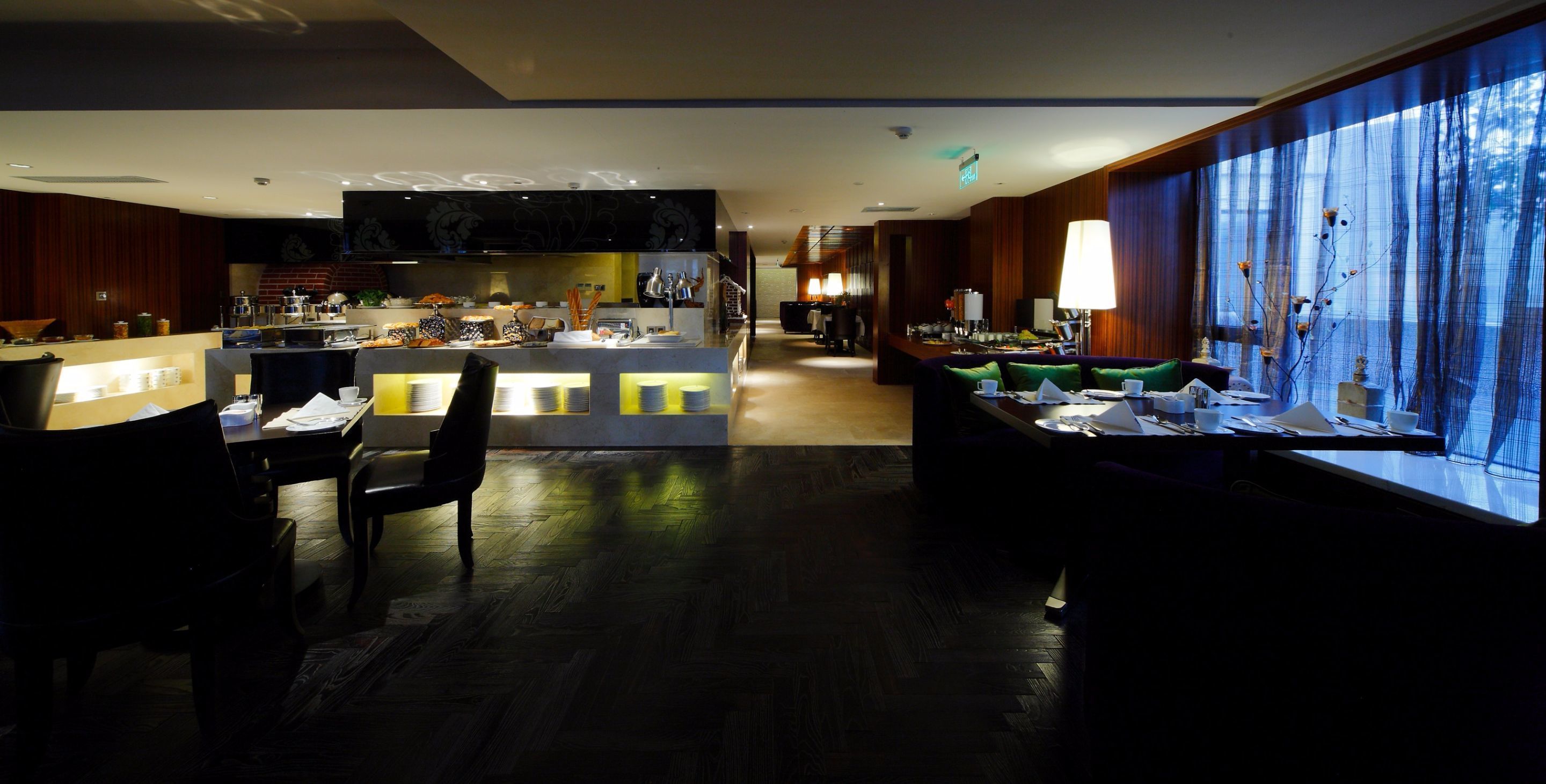 Um saguão de hotel moderno com área de bar central, espaços para sentar e uma grande janela com vista.
