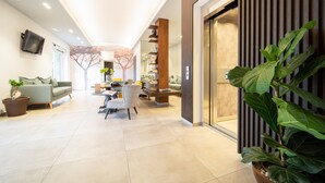 Um hall de hotel moderno com um sofá, poltronas, uma mesa de centro e uma grande planta em vaso.
