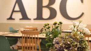 Uma mesa com um vaso de flores e uma placa com letras grandes ao fundo.