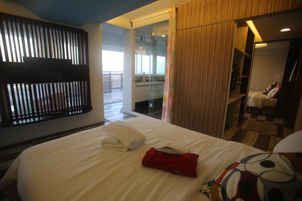Quarto de hotel com uma cama grande, um guarda-roupa, uma casa de banho com porta de vidro e vista para o exterior.