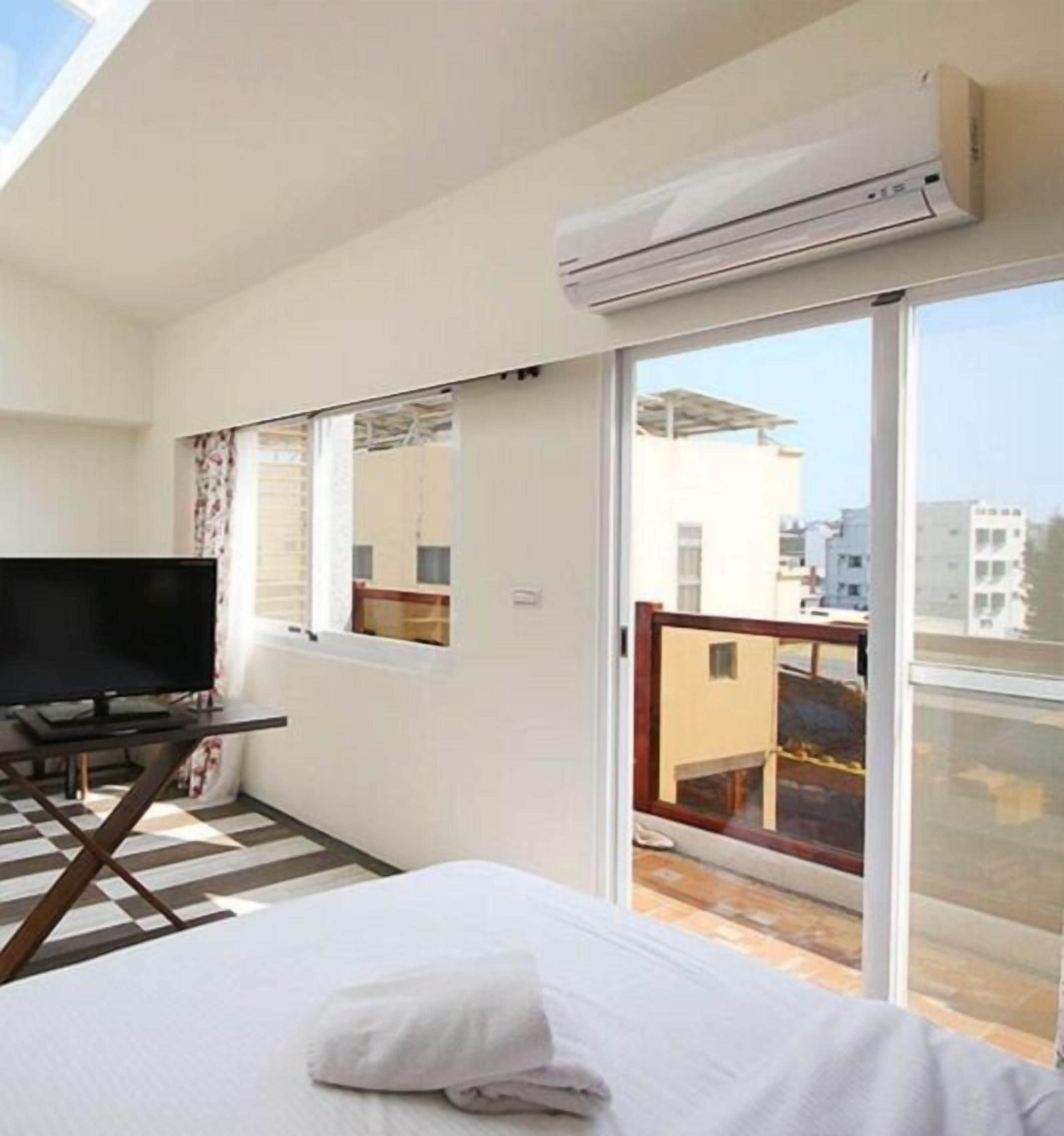 Quarto de hotel com cama, televisão e varanda com vista para edifícios.
