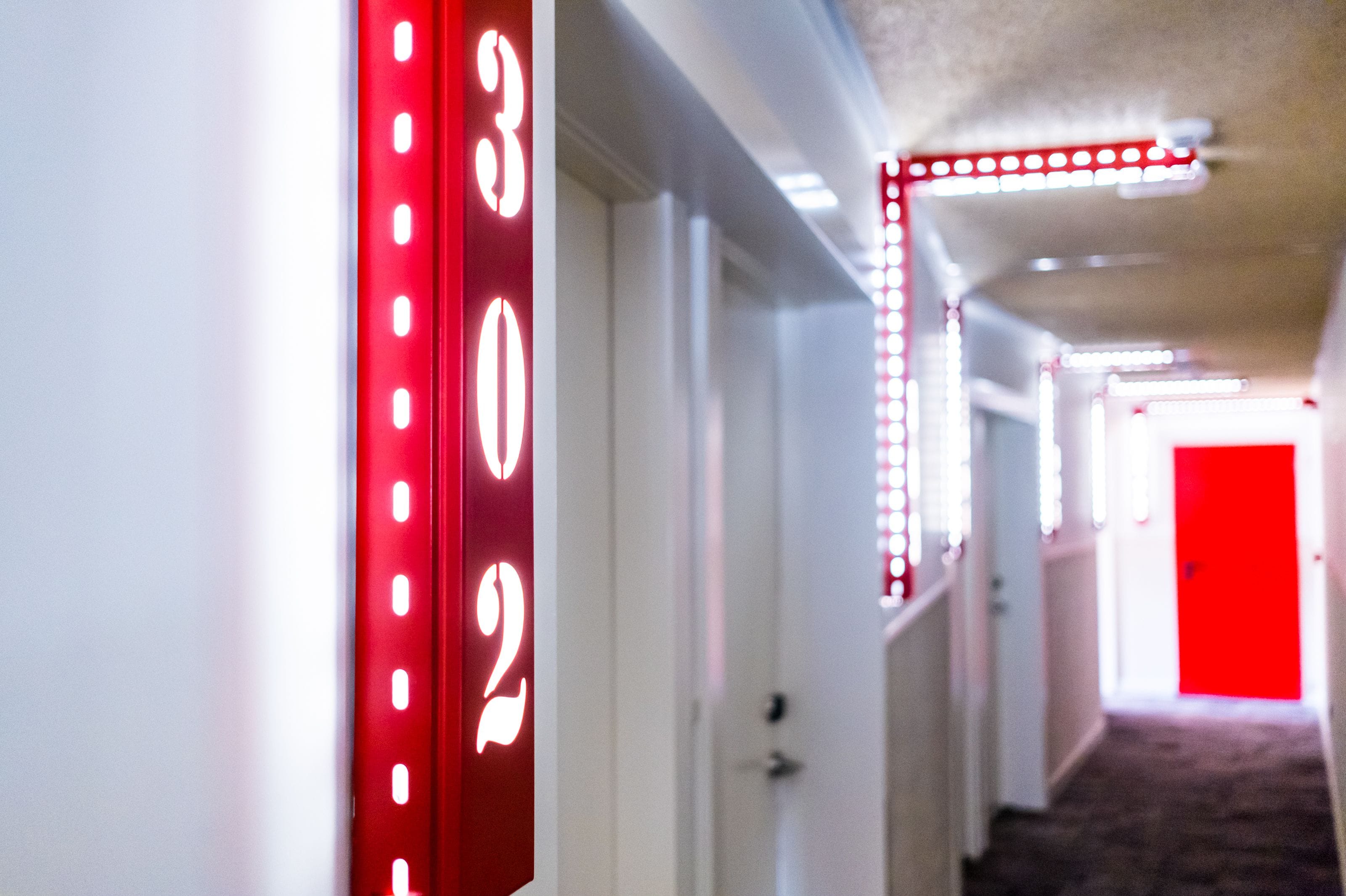Corredor iluminado por um letreiro de neon vermelho indicando o quarto 3022.